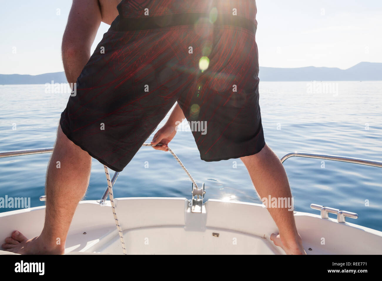 A young man on a boat pulling the rope of an anchor Stock Photo - Alamy