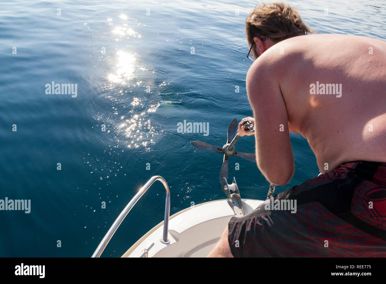 A young man on a boat pulling the rope of an anchor Stock Photo - Alamy