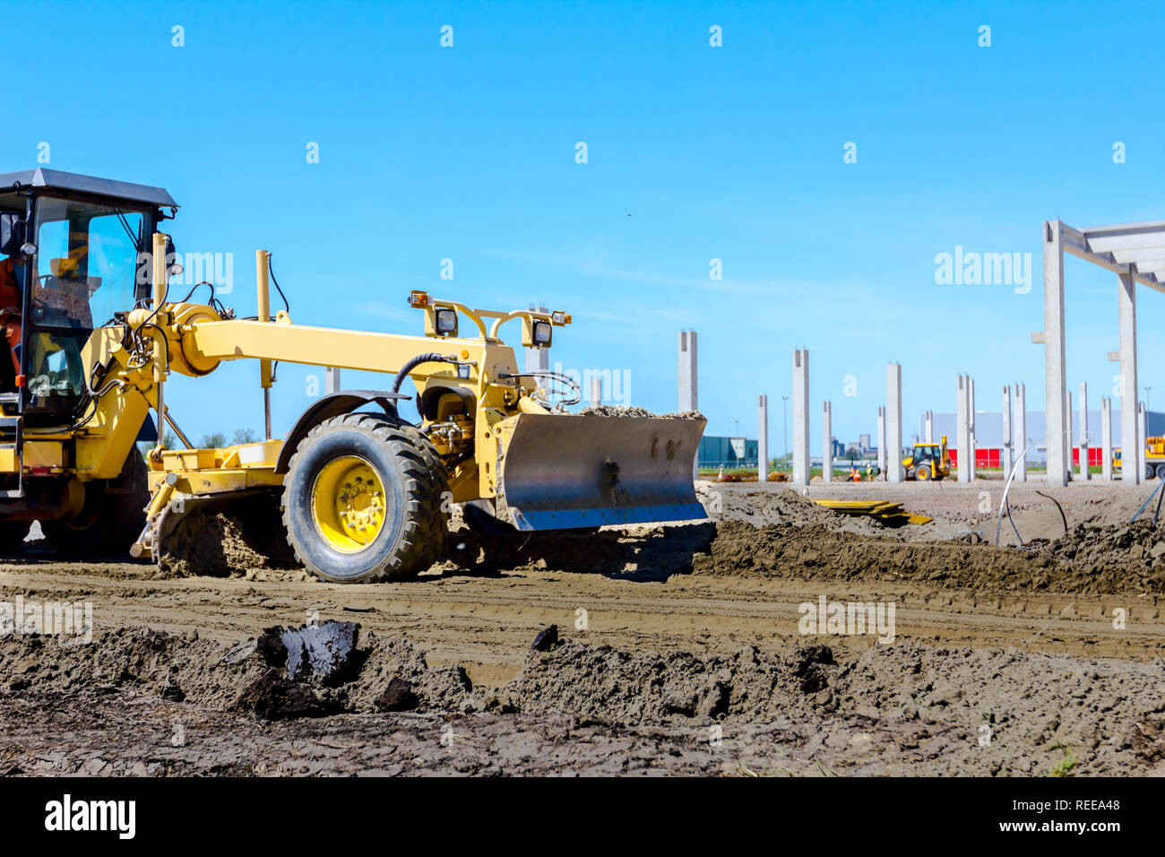Operator is driving yellow grader, leveling ground at building site ...