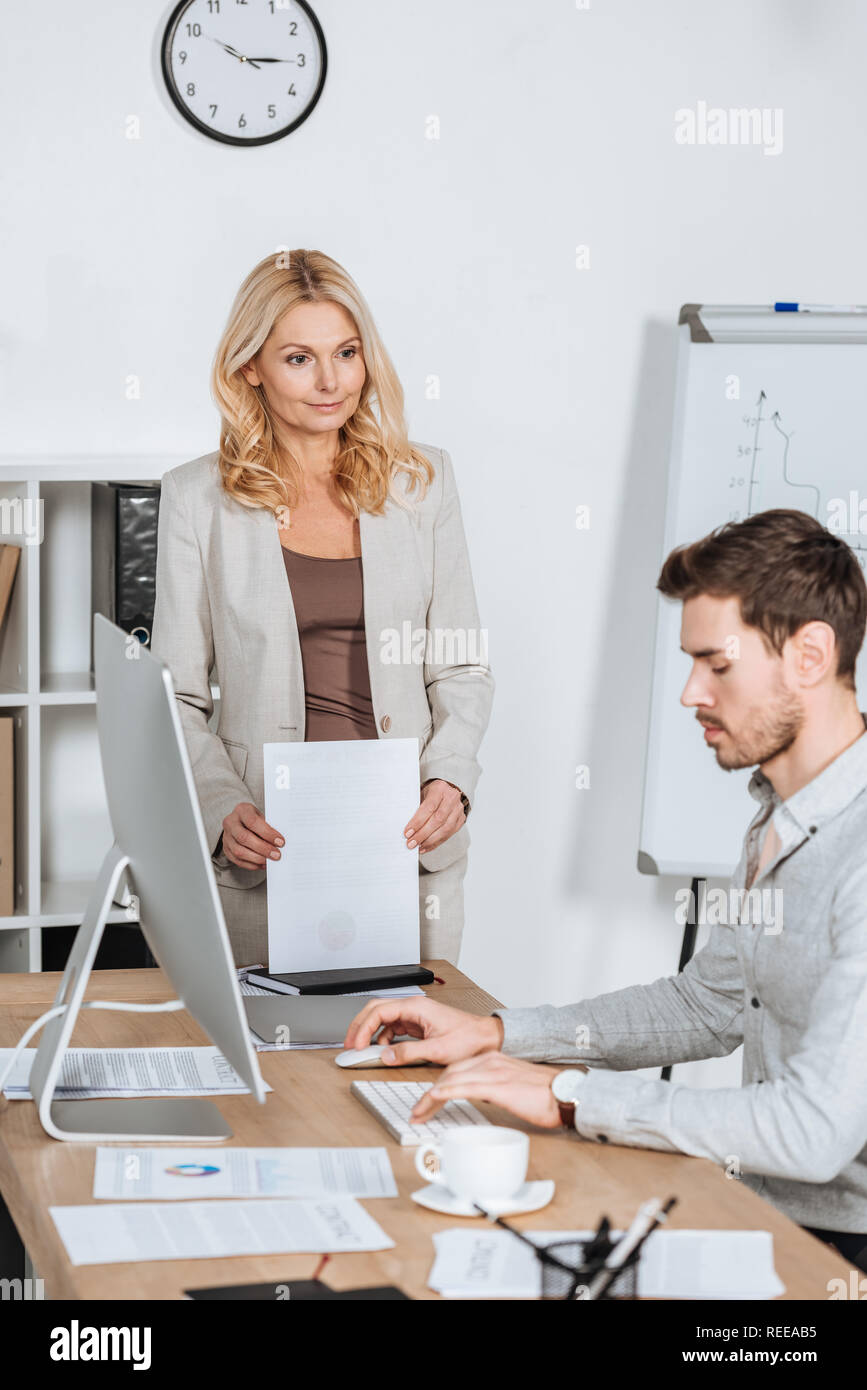 mature business mentor holding papers and looking at young businessman ...