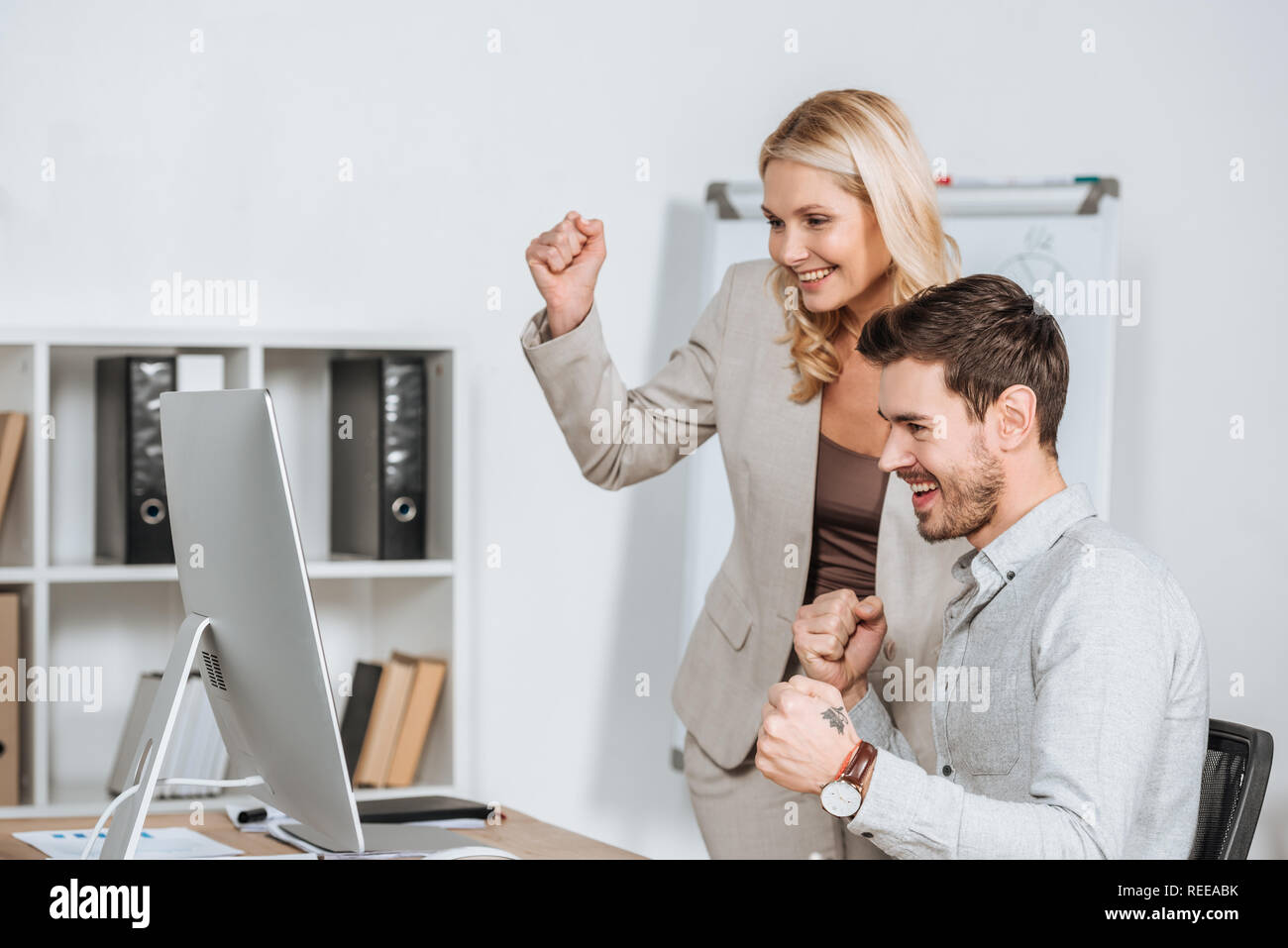 cheerful professional businesspeople triumphing and using desktop ...