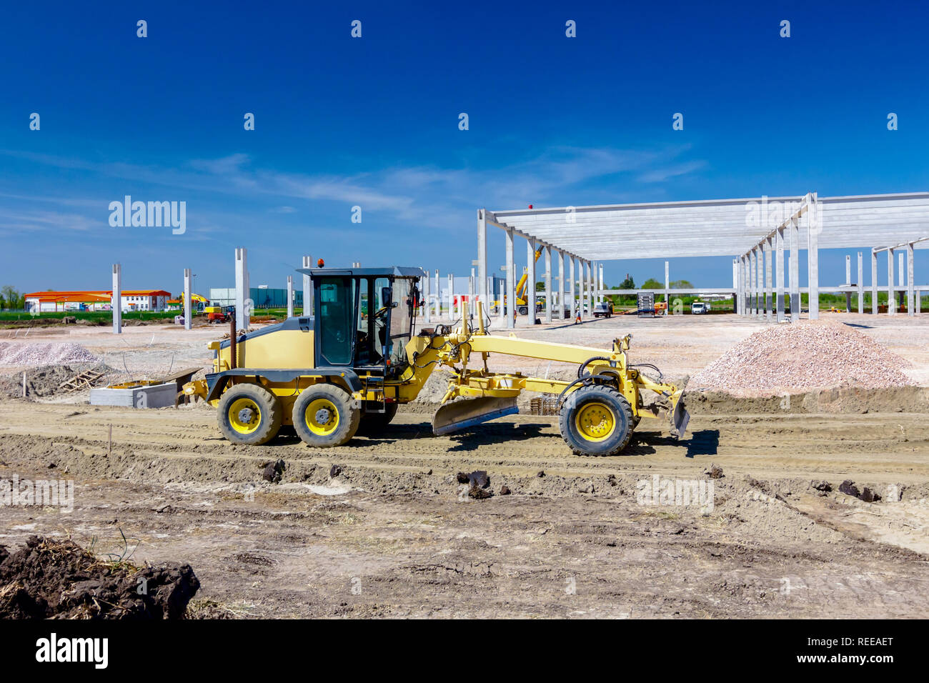 Operator is driving yellow grader, leveling ground at building site ...