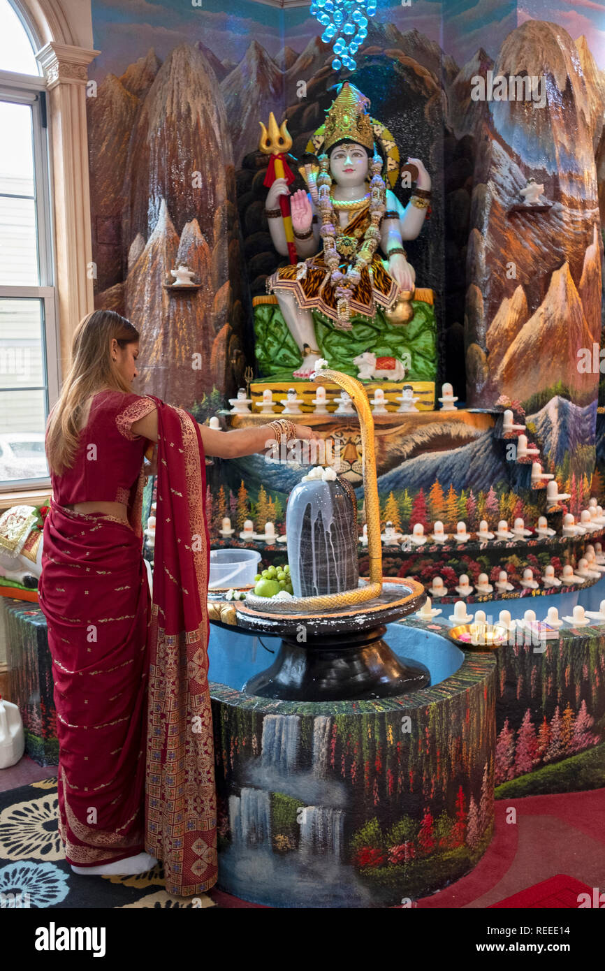 A young Hindu devotee pours milk over a lingam near a statue of Shiva ...