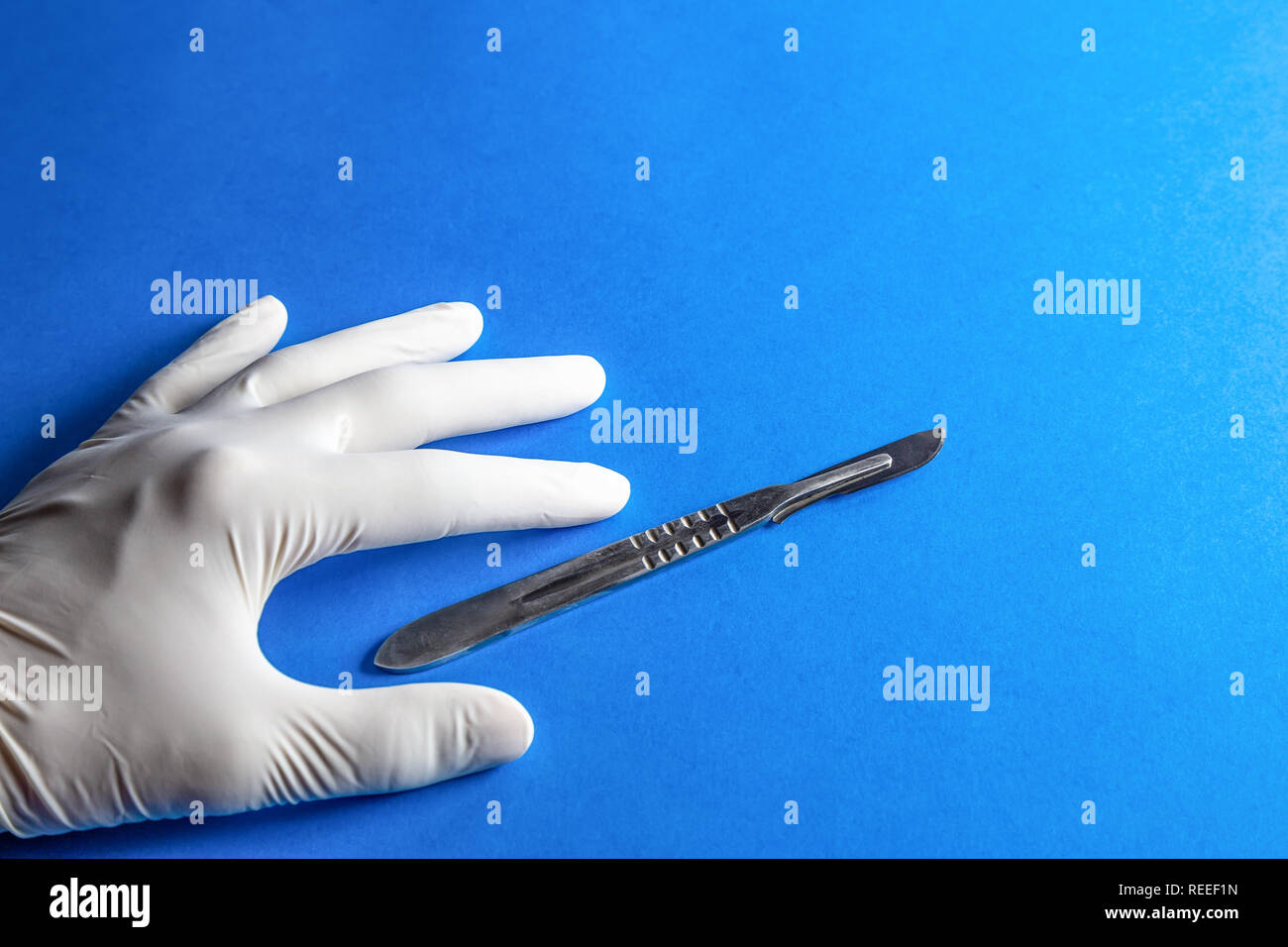 Scalpel in surgeon's hand over blue background. Hand holding a scalpel ...