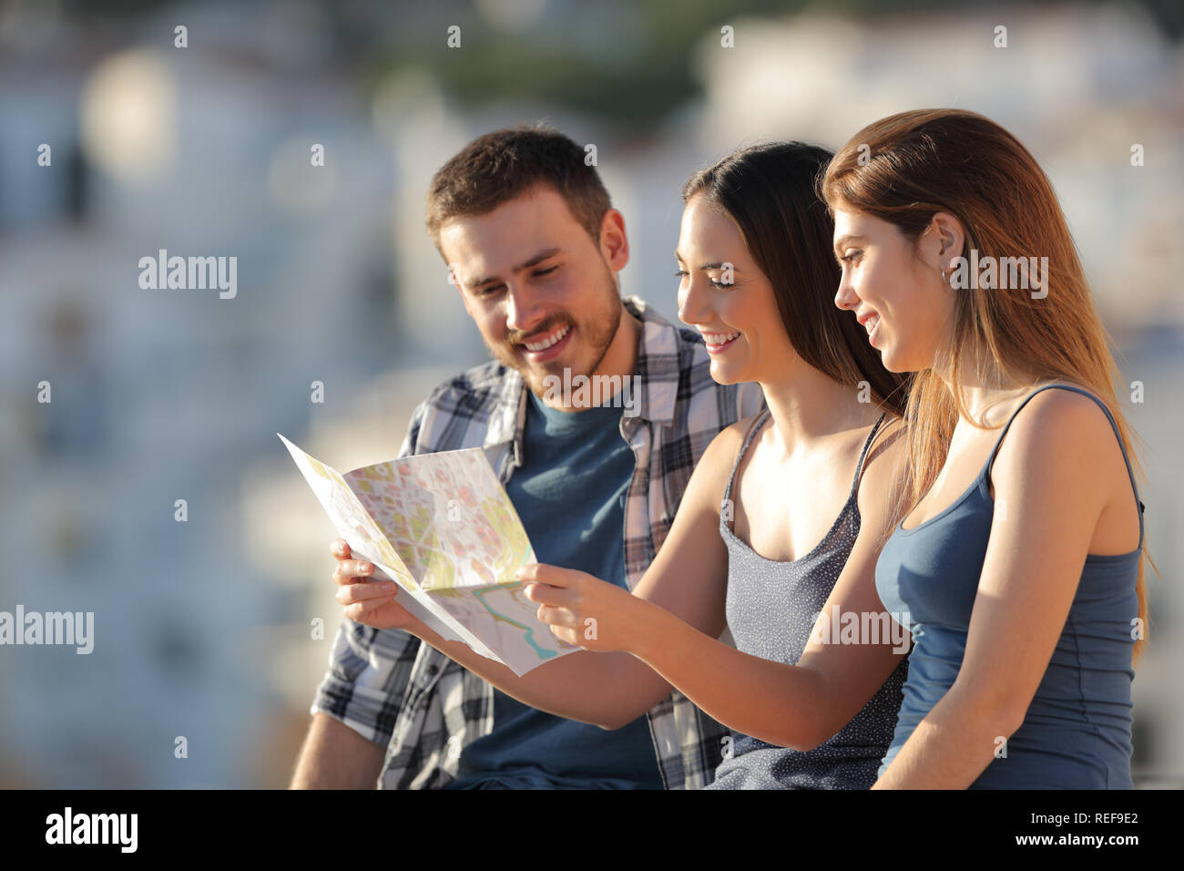Three happy tourists checking paper map in a town on vacation at sunset ...
