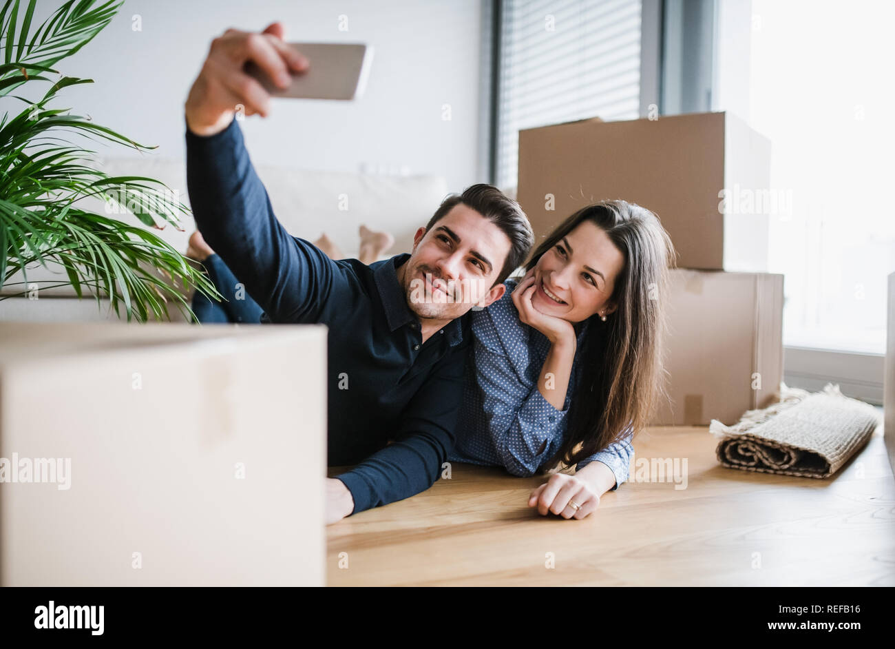 A young couple with a smartphone moving in a new home, taking selfie ...