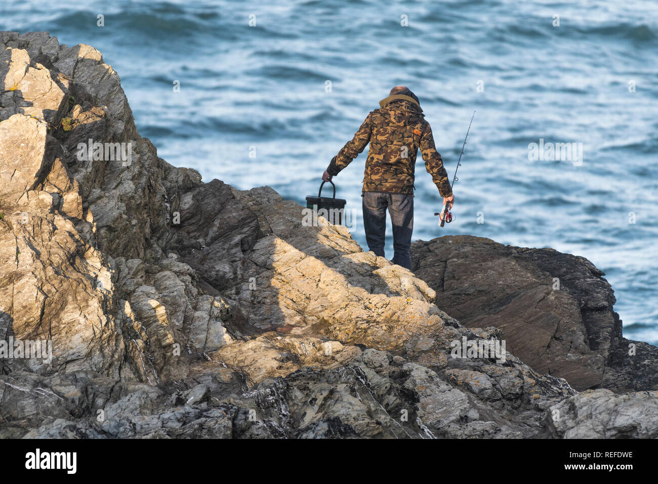 An angler walking over rocks looking for a fishing mark in Cornwall ...