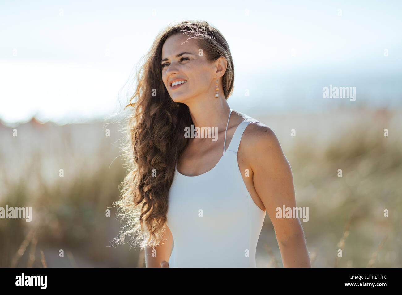 Portrait of smiling modern woman in white swimwear on the seashore ...