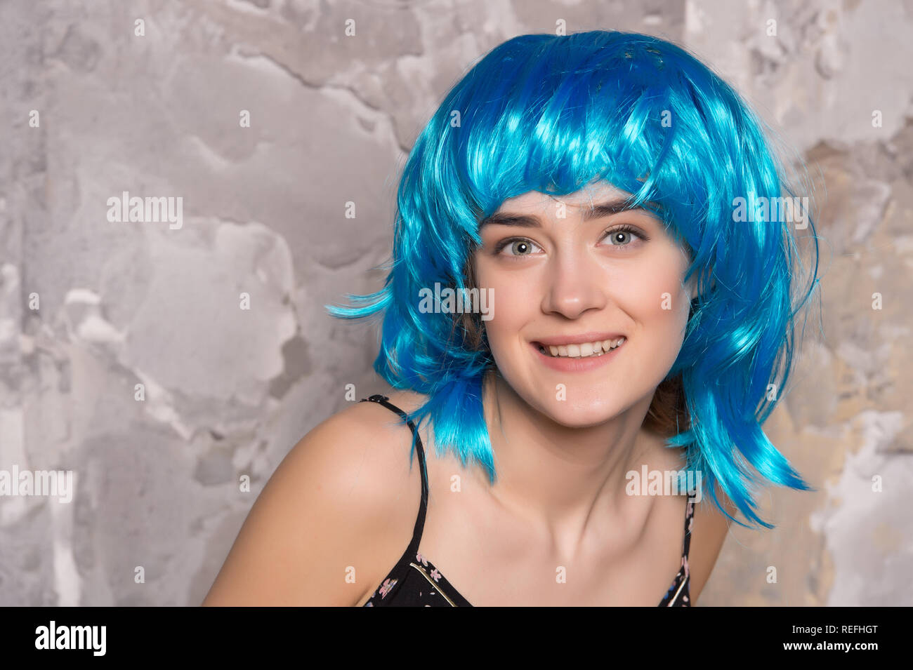 Freak concept. Lady on smiling face posing in blue wig, concrete wall ...