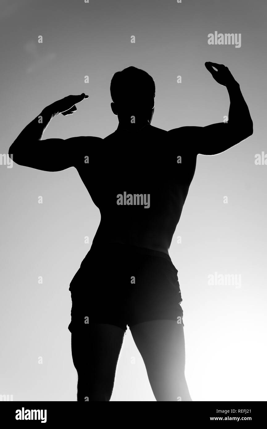 Bodybuilder posing on sky and sun light, back view. Athlete showing ...
