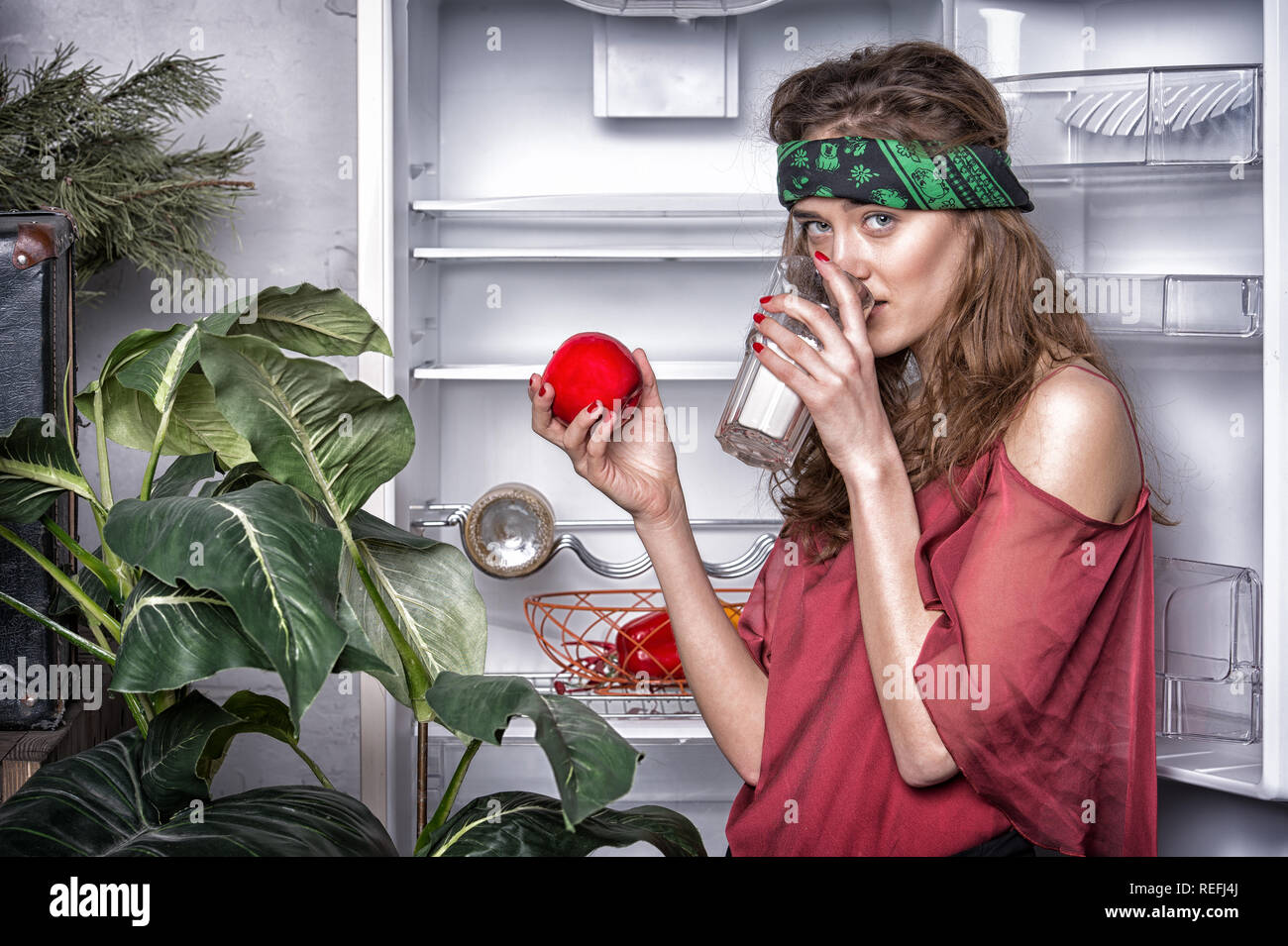 Lady on dreamy face stands in front of opened empty fridge and drinks ...