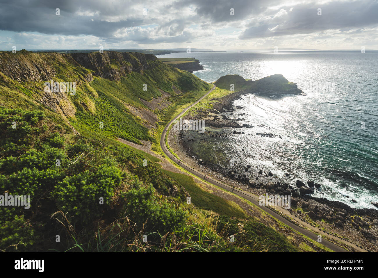 Sunlit ocean, green shore with the road. Northern Ireland landscape ...