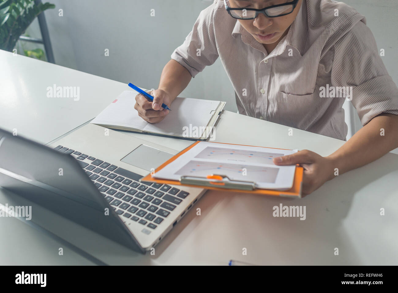 Young Asian man reading report and writing note Stock Photo - Alamy