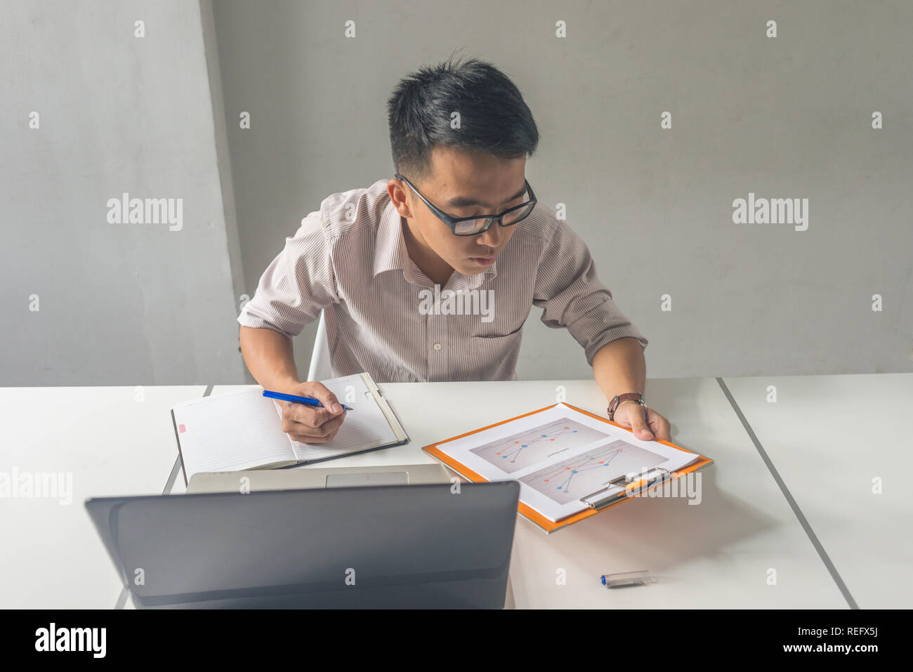 Asian man reading report and take note Stock Photo - Alamy