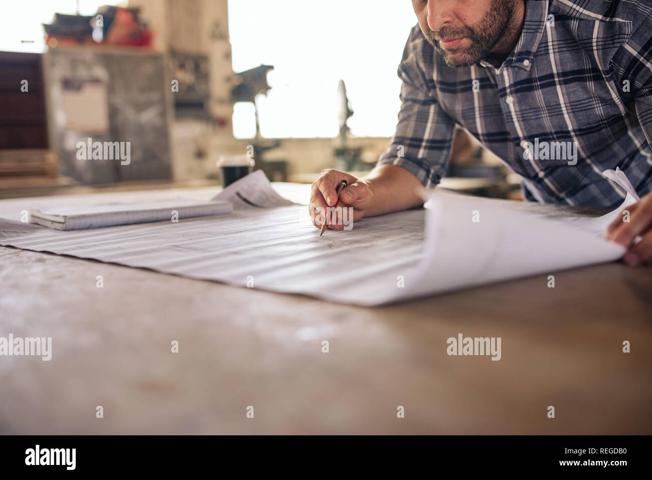 Woodworker leaning over a bench reading furniture design blueprints ...