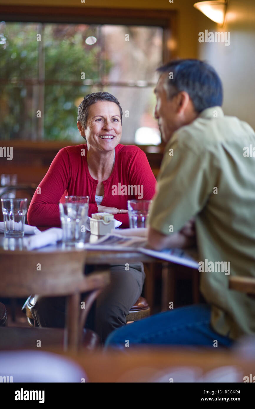 Smiling mid-adult woman looking across a table at a man while sitting ...