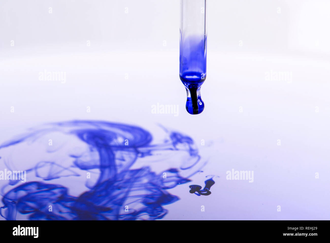 Pipette with blue liquid dripping into water Stock Photo - Alamy