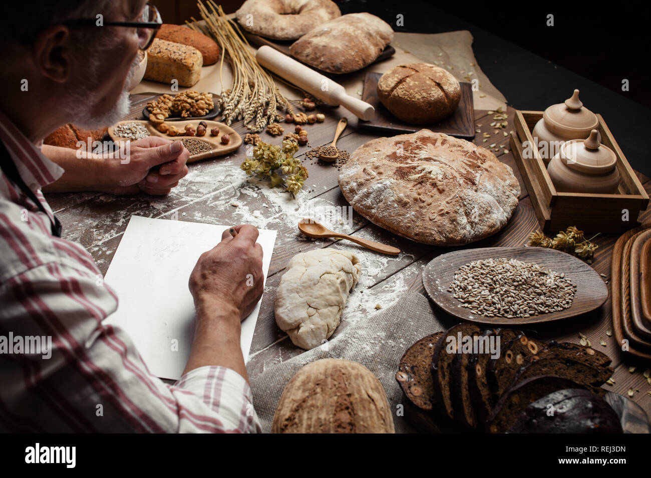 Old Baker writing down old-time recipe in bakery notebook surrounded by ...