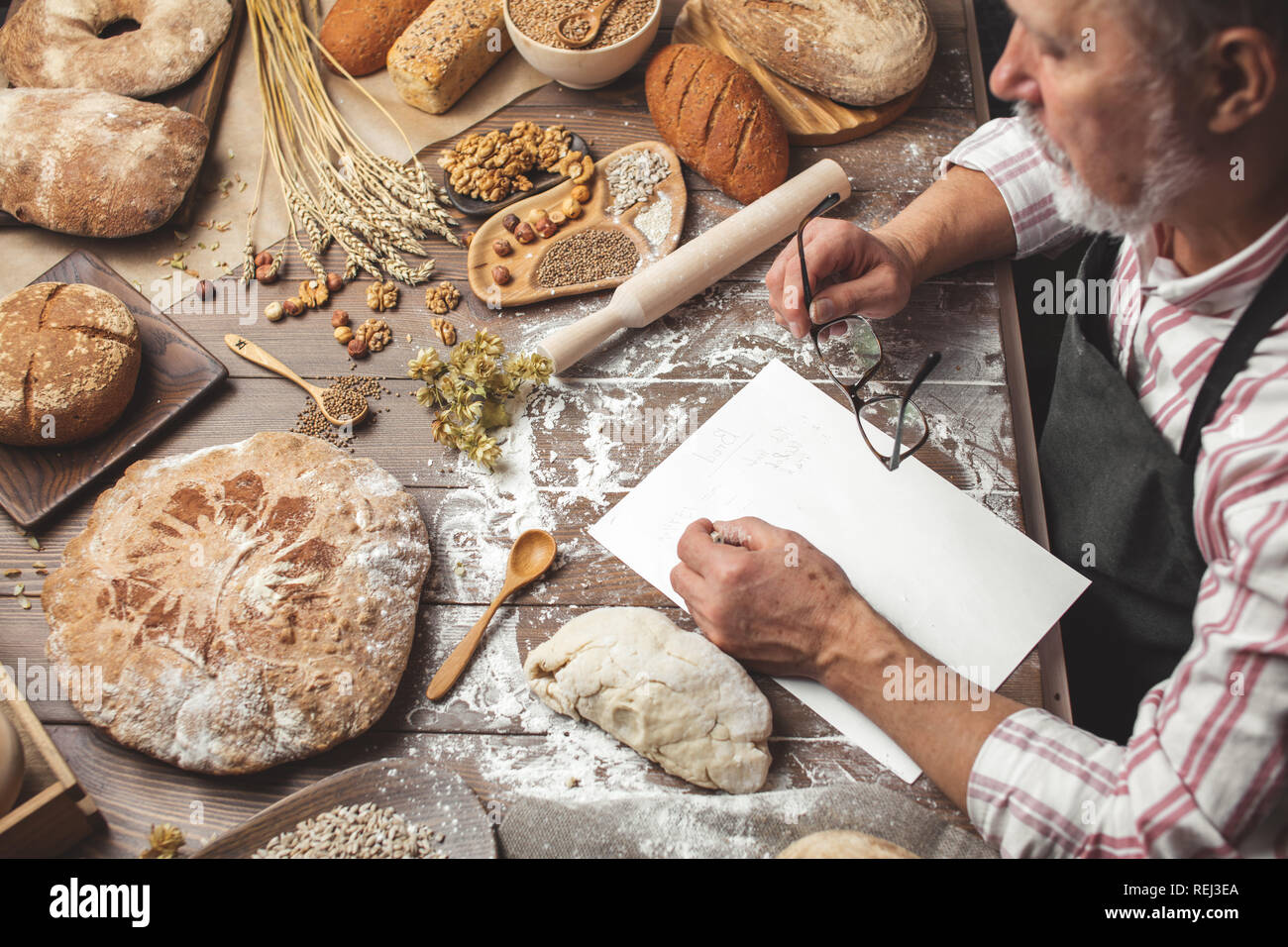 Old Baker writing down old-time recipe in bakery notebook surrounded by ...