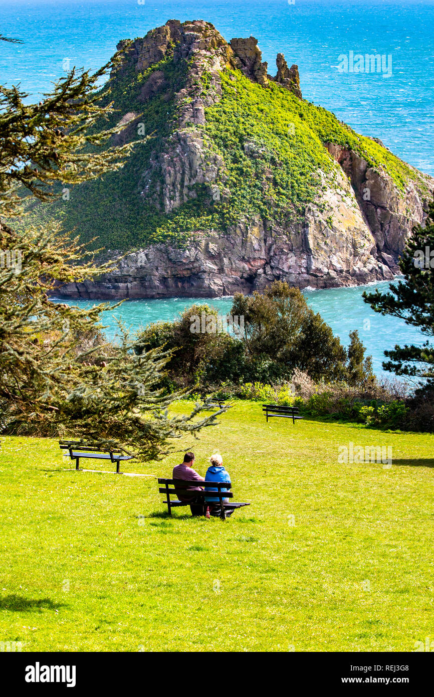 A couple sitting on a bench looking out to sea and the view of Thatcher ...