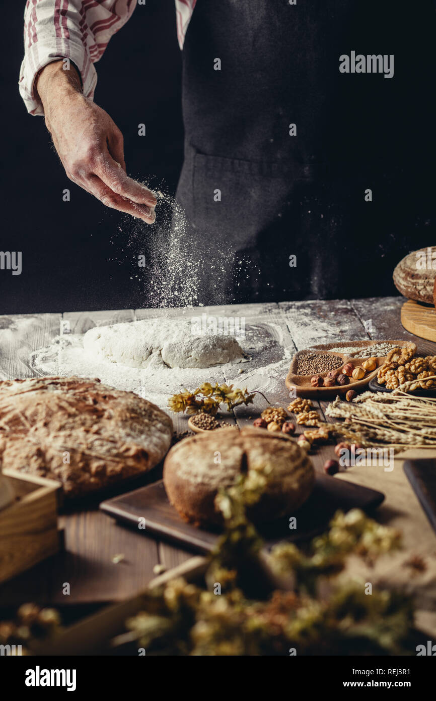 Man sprinkling some flour on dough. Hands kneading dough, cropped view ...