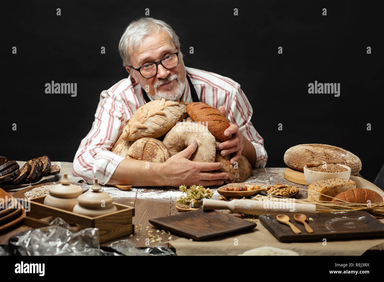 Happy old baker looking at camera and smiling while hugging loaves of ...