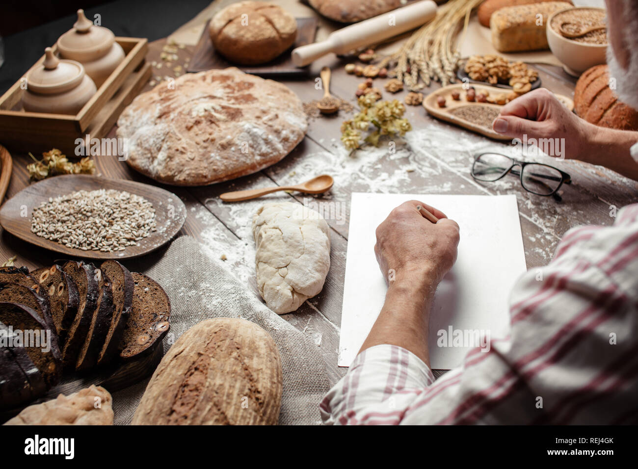 Old Baker writing down old-time recipe in bakery notebook surrounded by ...