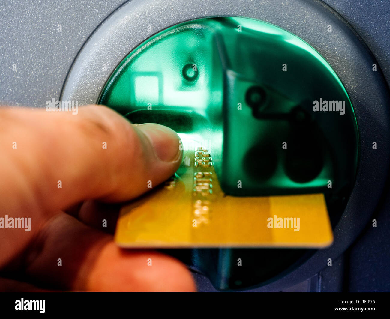 Close-up of an adult man's hand inserting a debit card into the slot of an automatic teller ...