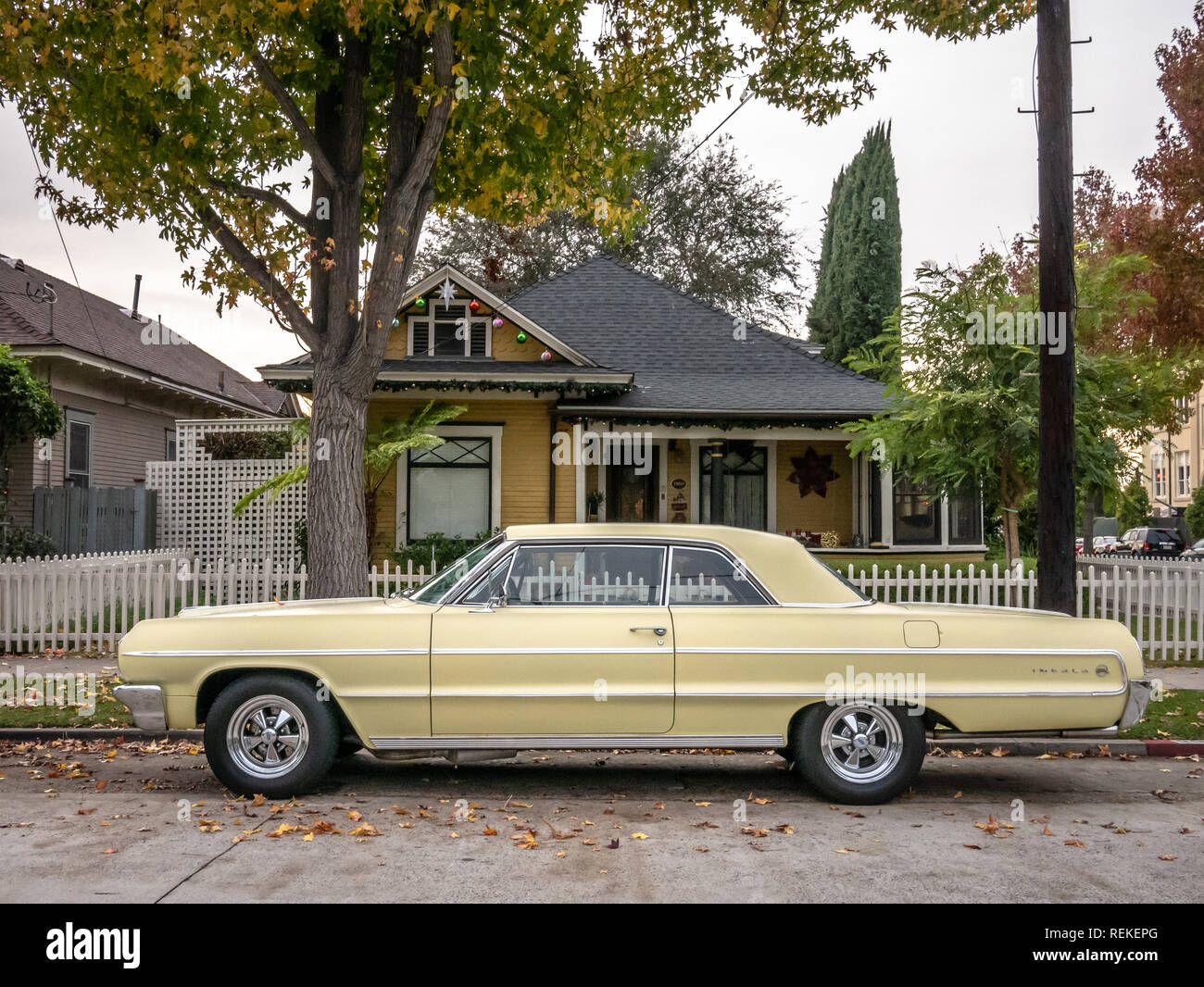 A classic yellow Chevy Impala parked in front of a cozy downtown house ...