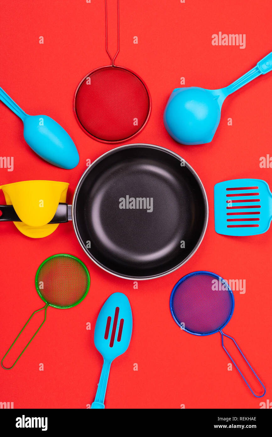 Frying pan in the center with cooking utensils around isolated on red ...