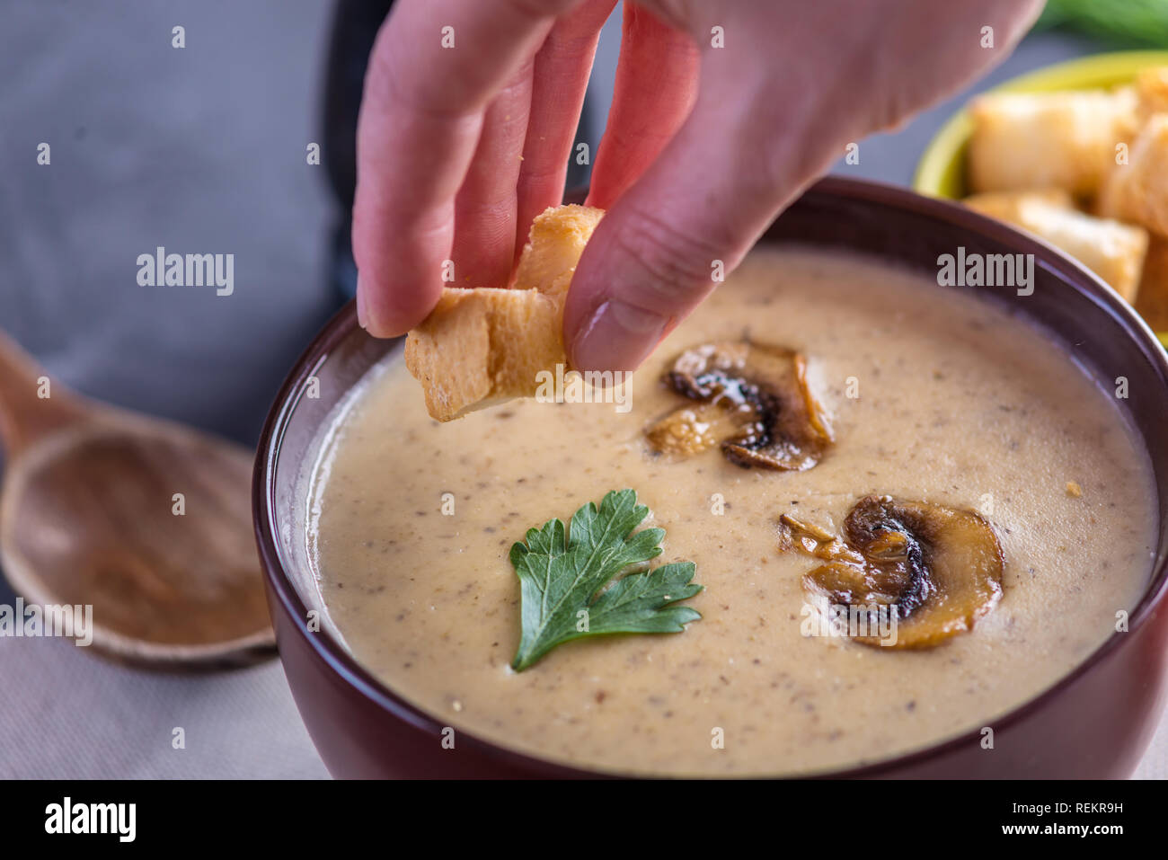 Female hand throwing crackers in cream of mushroom soup. Dark ...