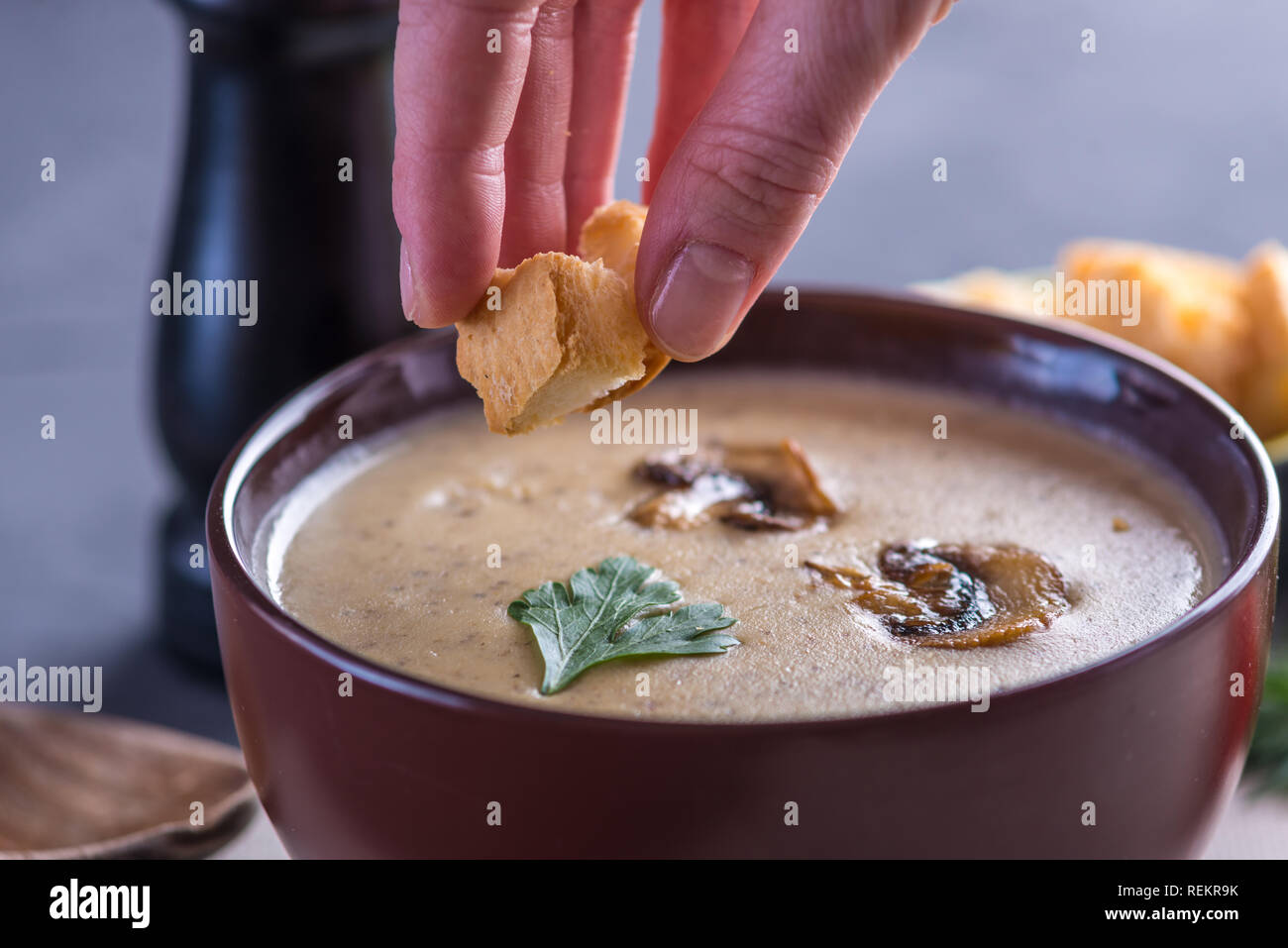 Female hand throwing crackers in cream of mushroom soup. Dark ...