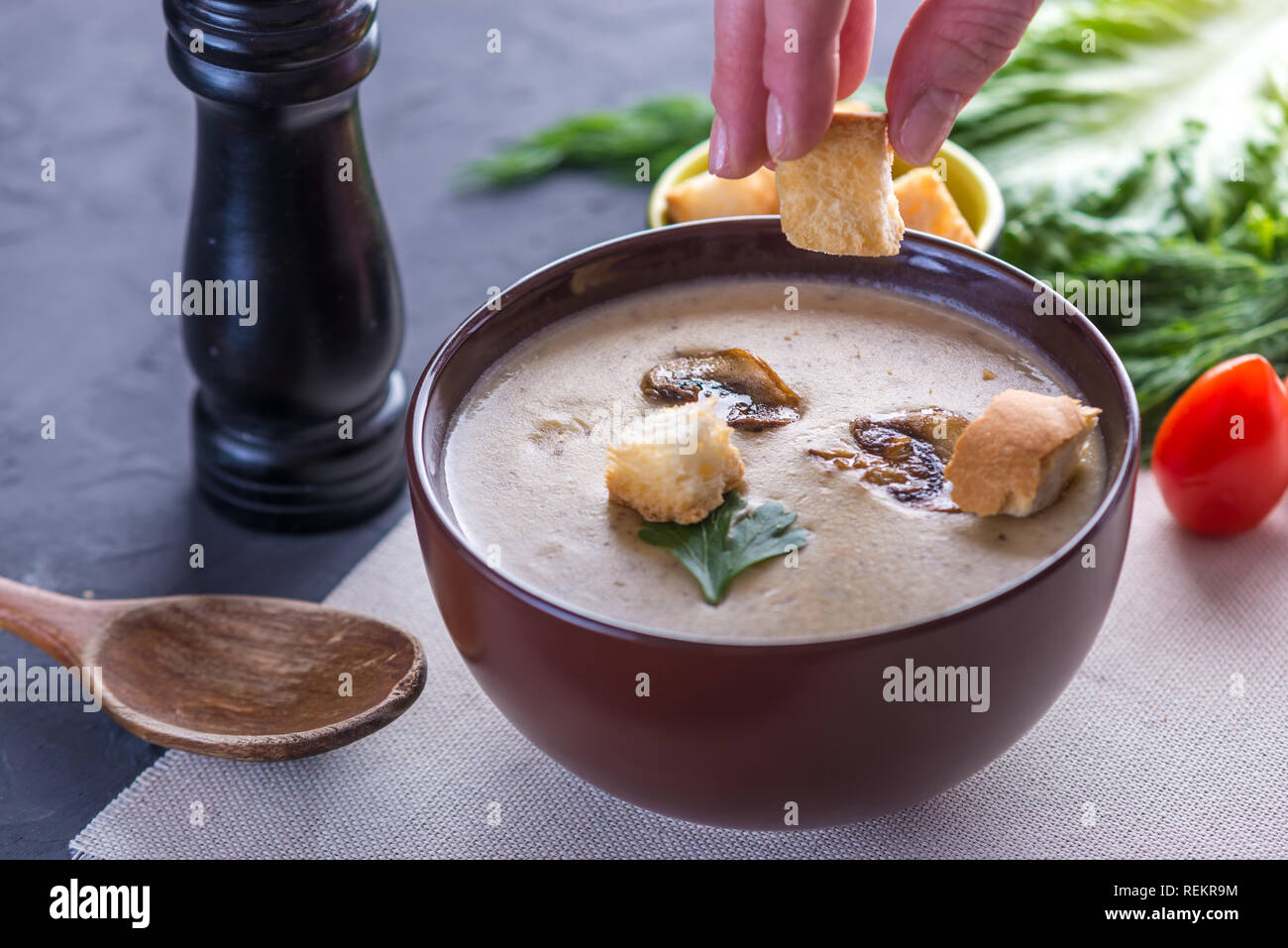 Female hand throwing crackers in cream of mushroom soup. Dark ...