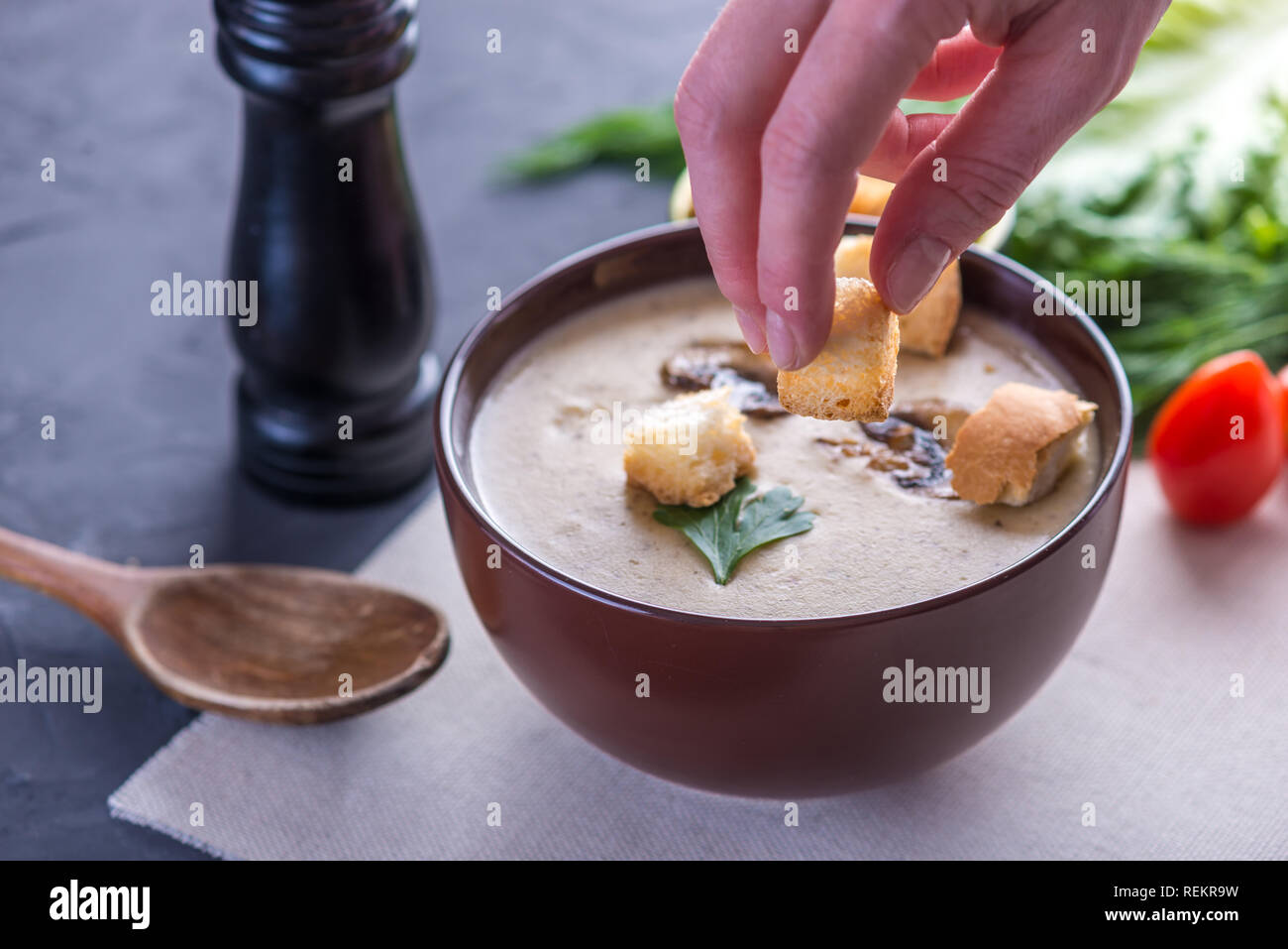Female hand throwing crackers in cream of mushroom soup. Dark ...
