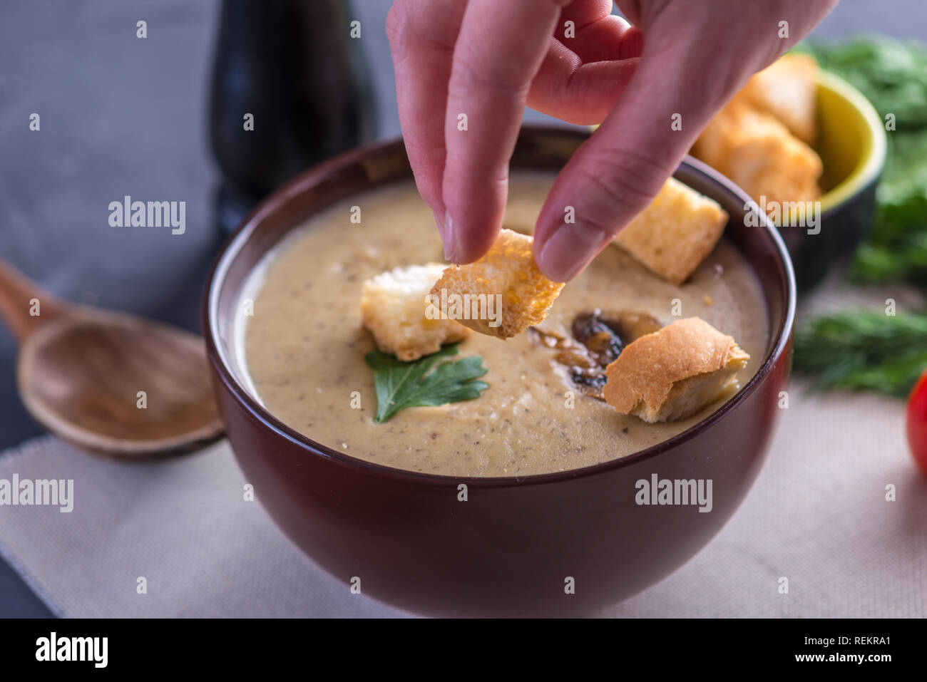 Female hand throwing crackers in cream of mushroom soup. Dark ...