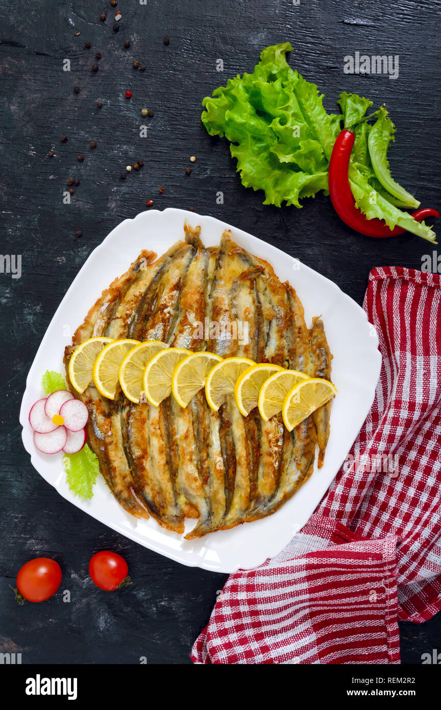 Fried capelin with lemon on a white plate on a black wooden background ...