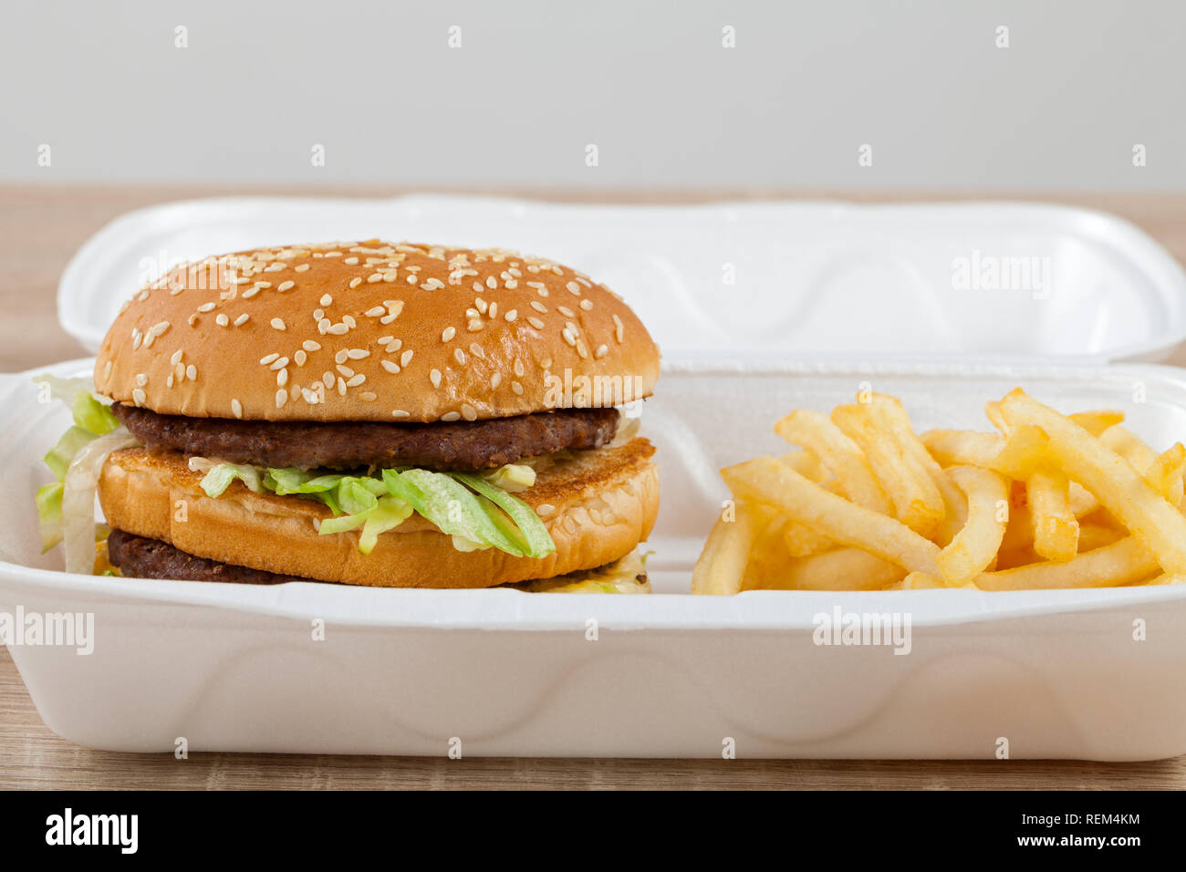 Fresh double cheeseburger and potato fries in a white plastic takeaway ...