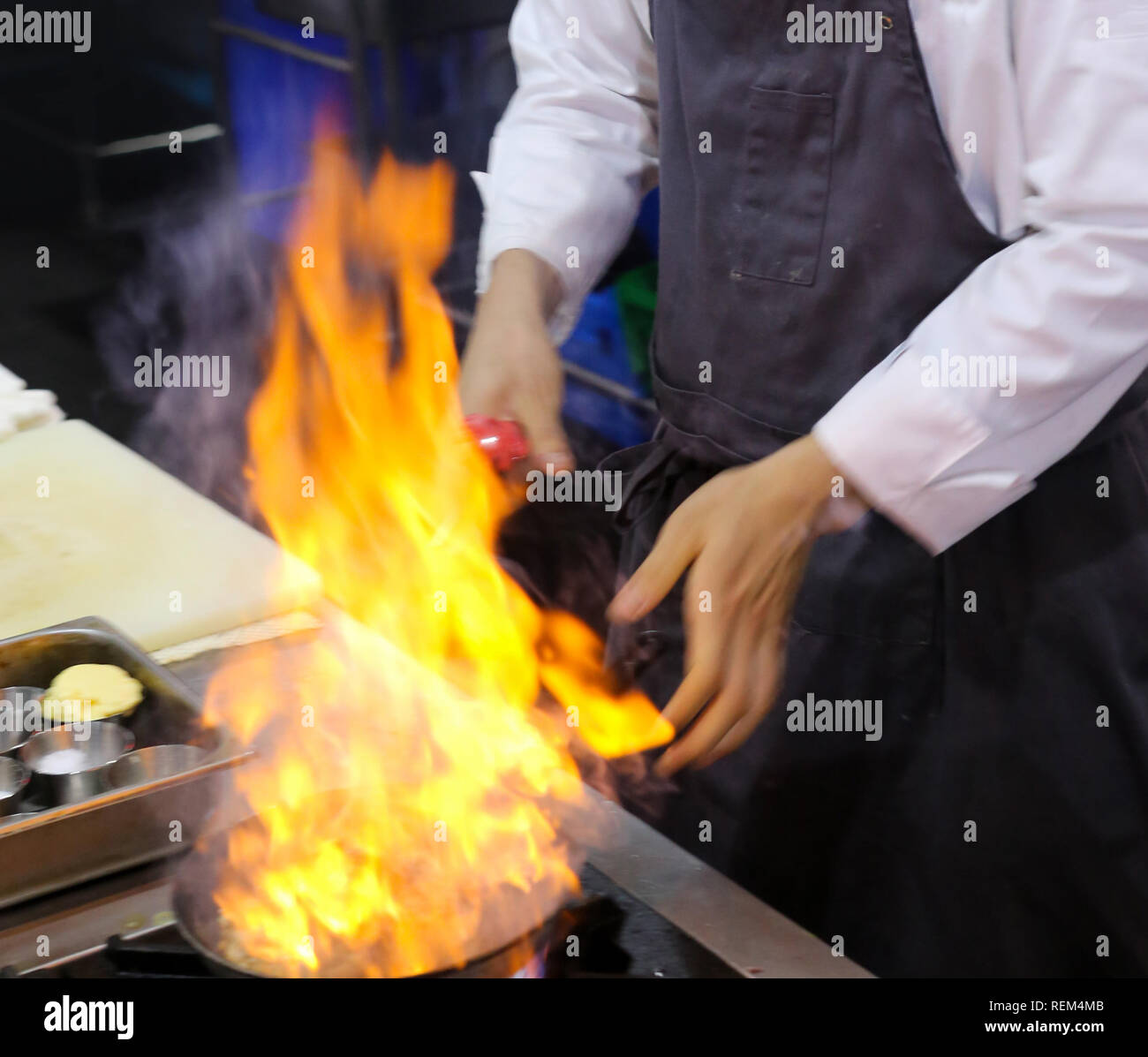 Chef in restaurant kitchen at stove with pan, doing flambe on food ...