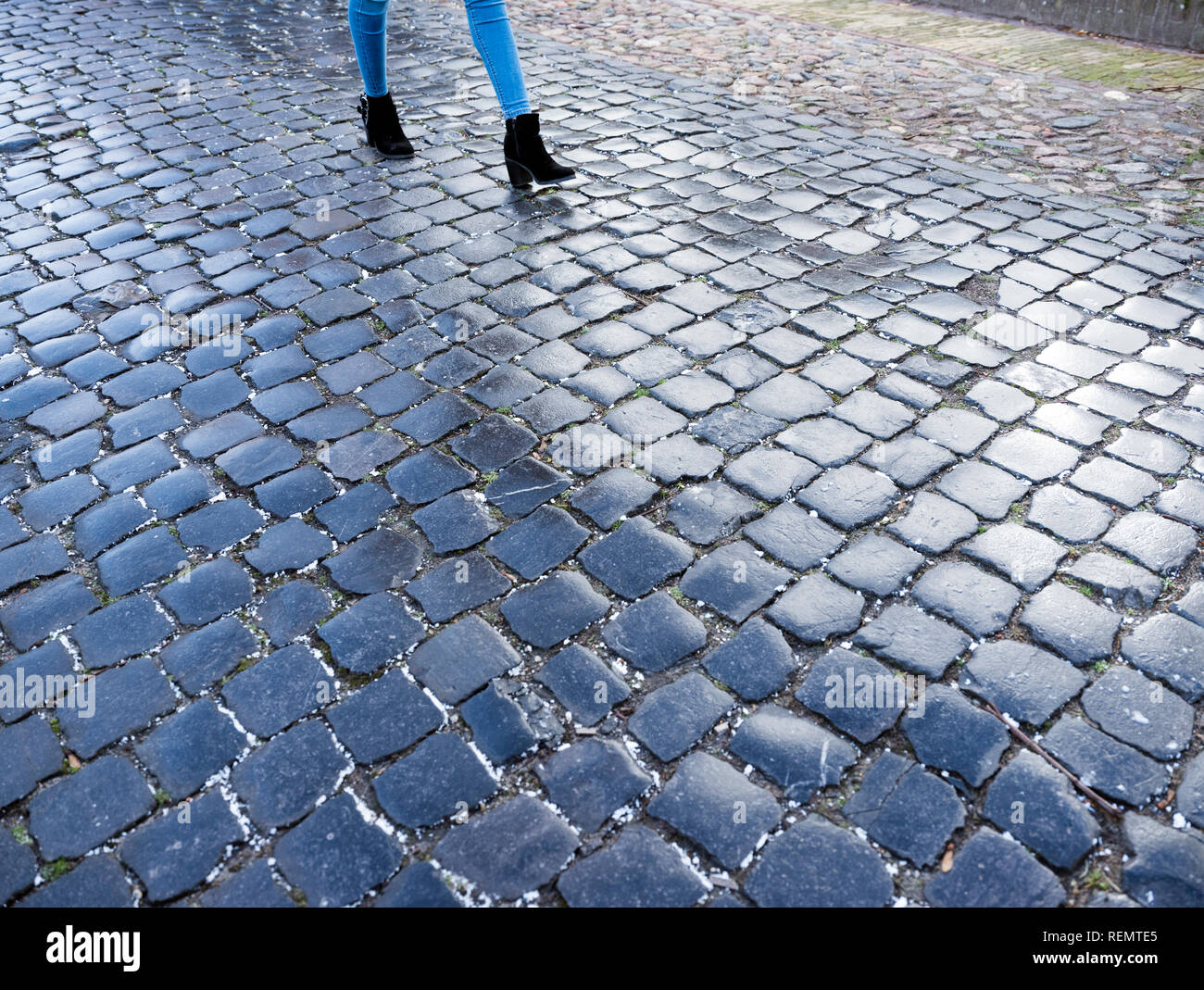 female legs in jeans and heel boots on old wet cobblestone street after ...