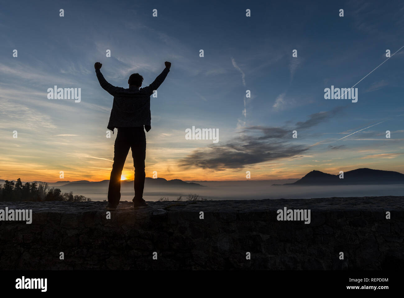 Young man standing on an old wall under glorious evening sky with his ...