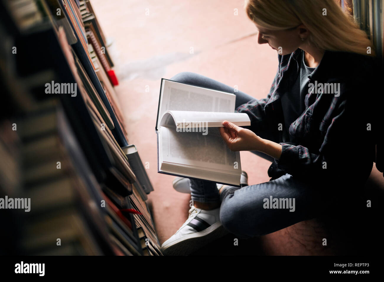 Young girl sitting on the floor in library between bookshelves, reading ...