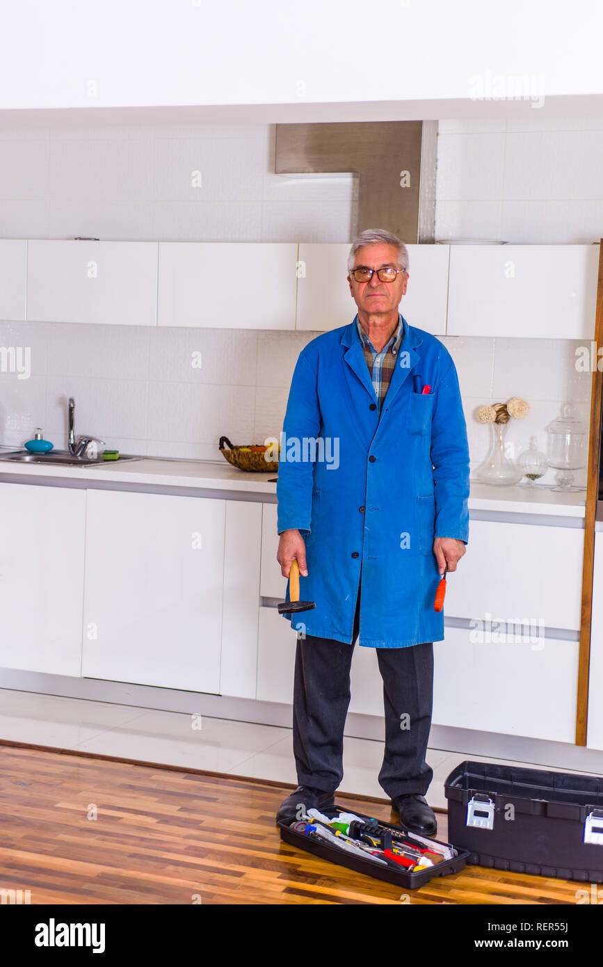An old age handyman standing near toolbox in the kitchen while holding ...