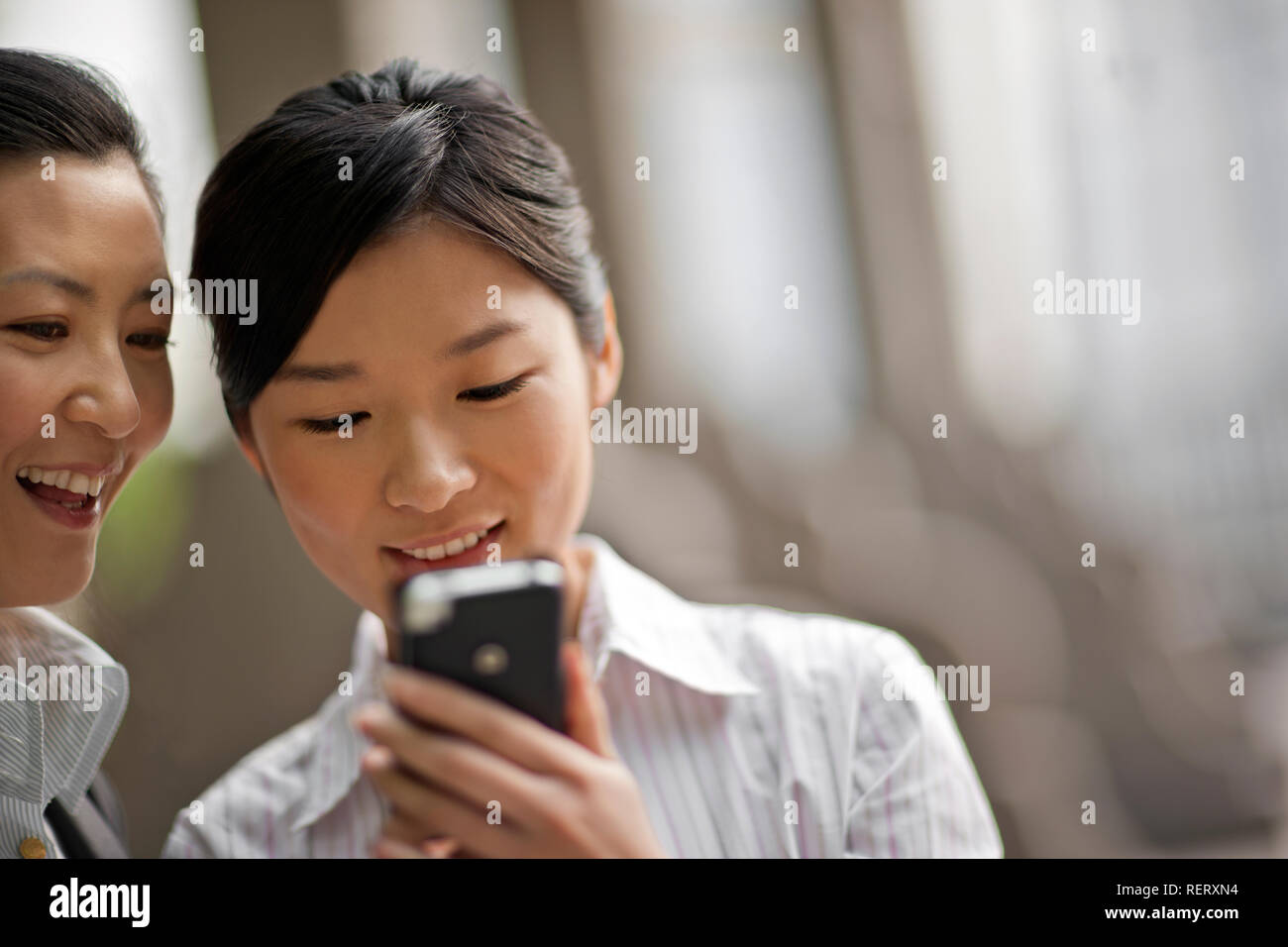 Two smiling friends looking at a cell phone Stock Photo - Alamy