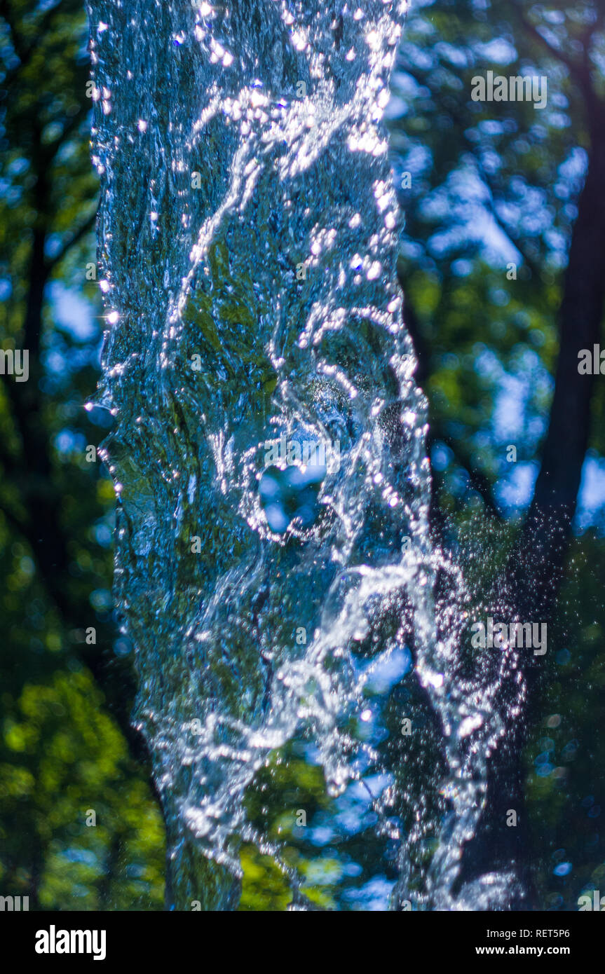 transparent falling water vertical flows against a blue sky and green ...