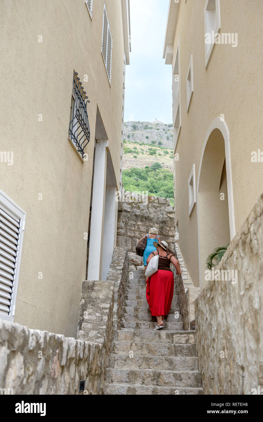 Two women are climbing steps in narrow gap between building in Sveti ...