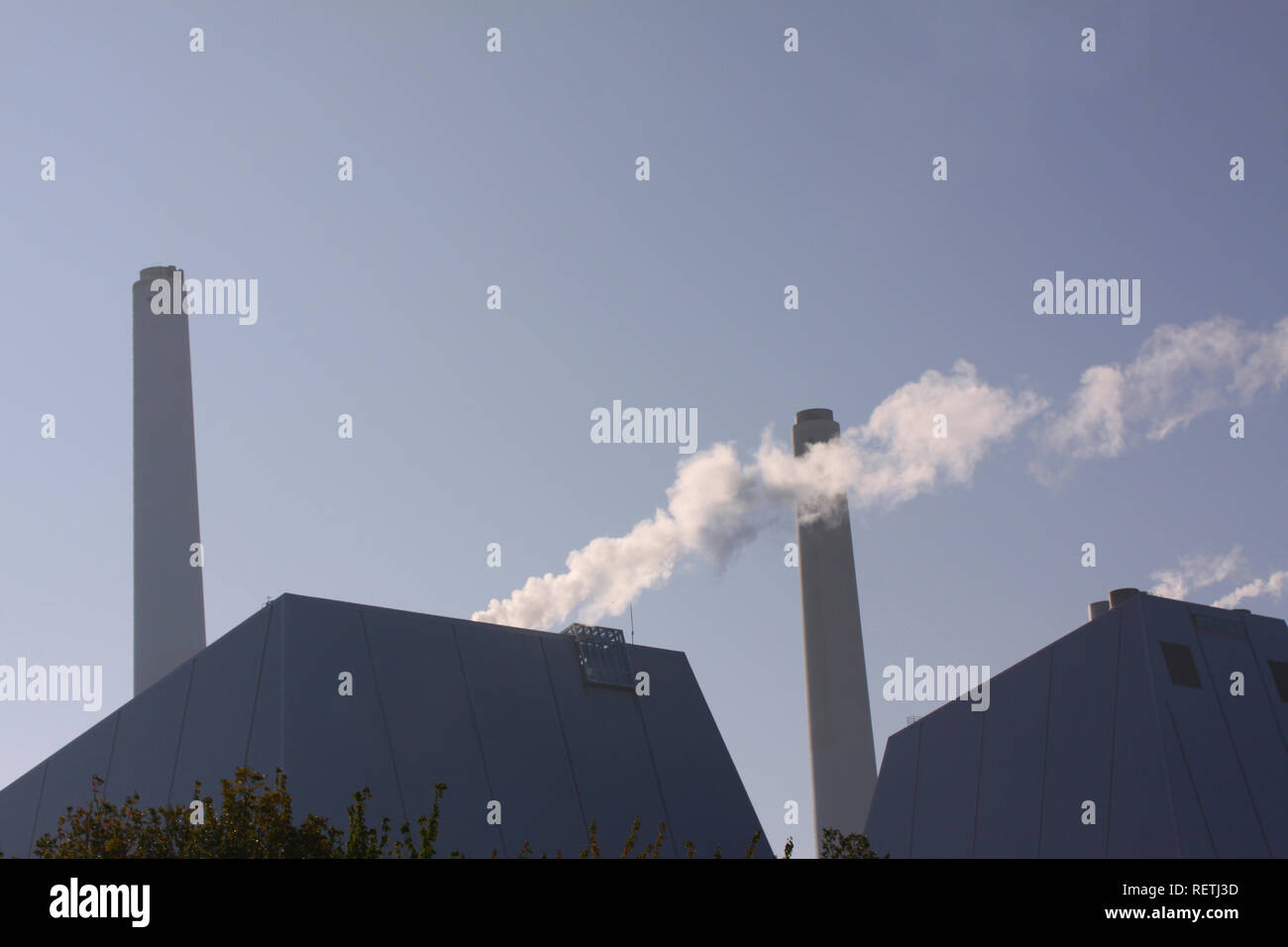 Modern power plant with chimney and column of smoke backlit against a ...