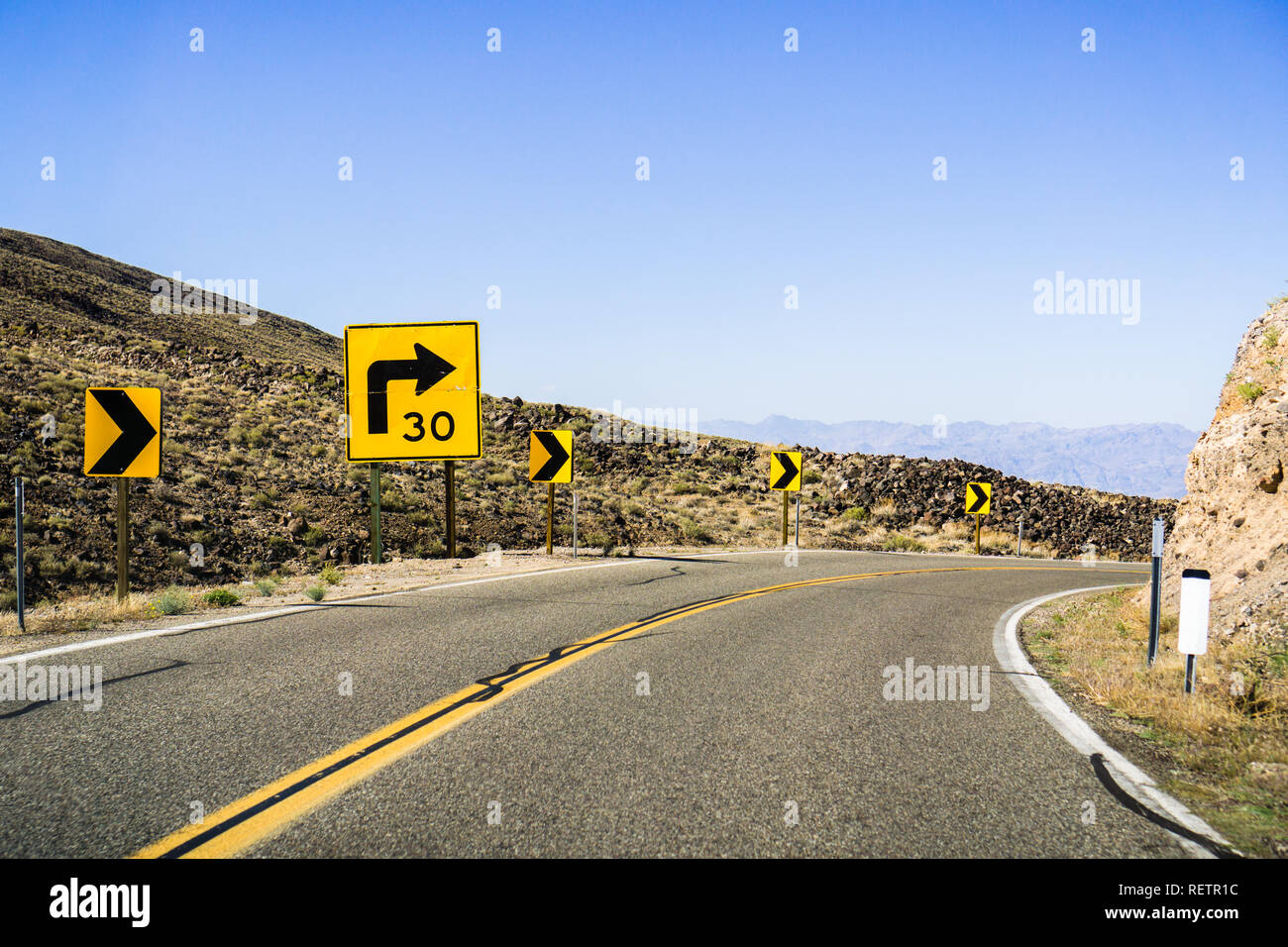 Steep right turn on a winding road; posted sign showing a 30 mph ...