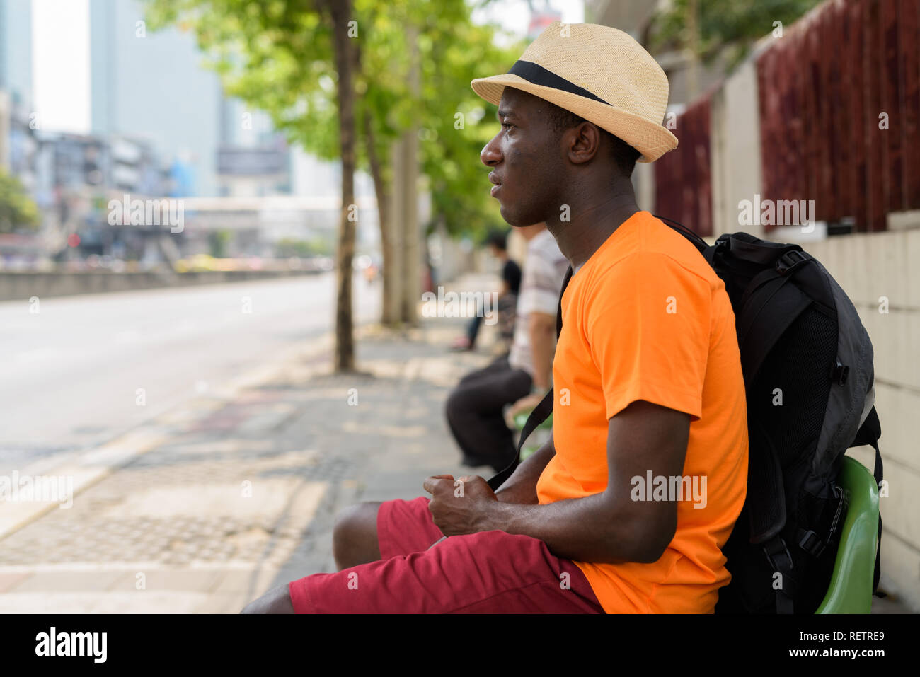 Young happy black African tourist man sitting at bus stop Stock Photo ...