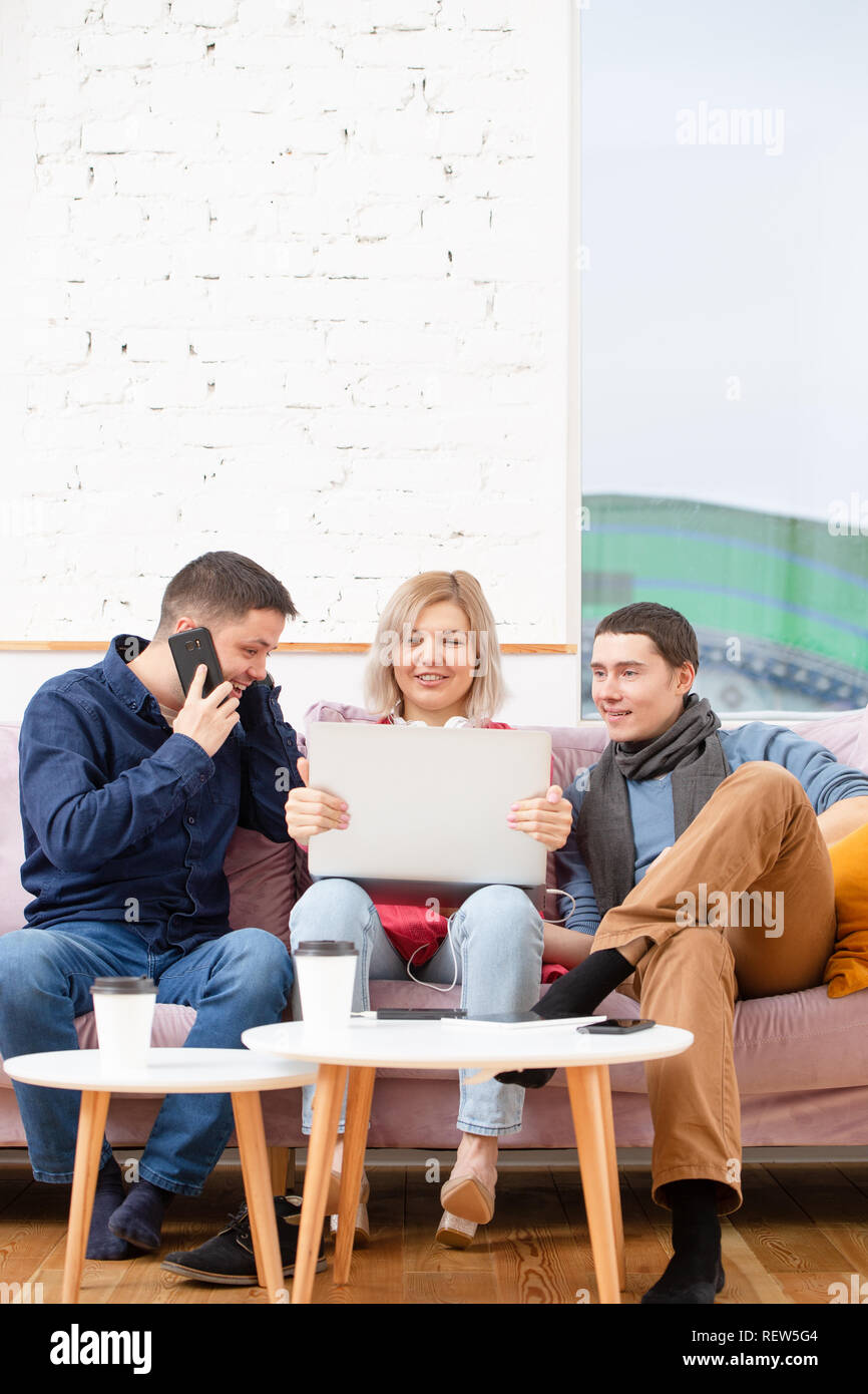 Friends sit on the couch, chatting and using a smartphone, desktop ...
