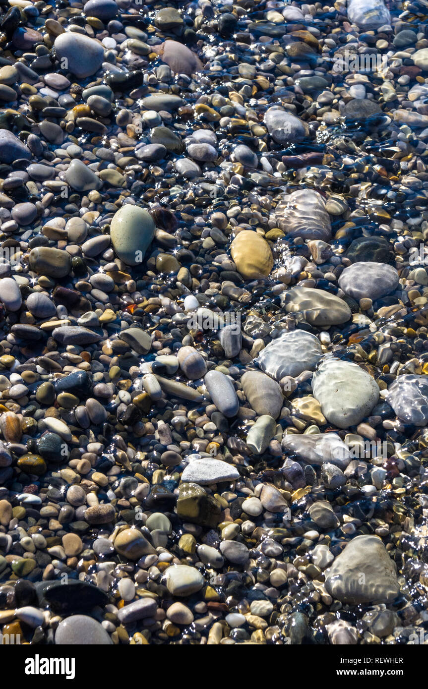 sea pebble beach with multicoloured stones, transparent waves with foam ...